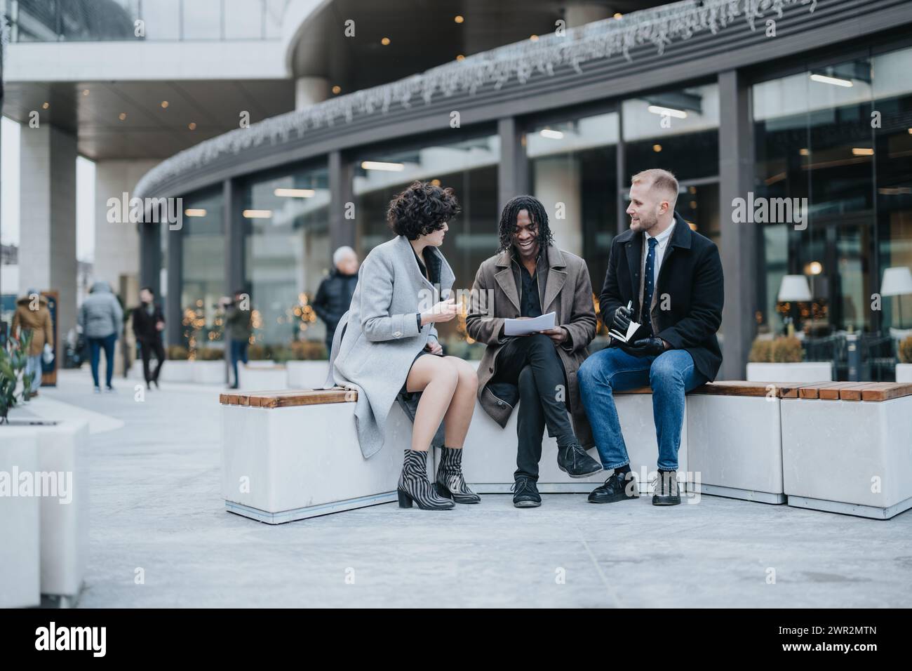 Three business colleagues discussing work-related matters while sitting on a bench outside an ...