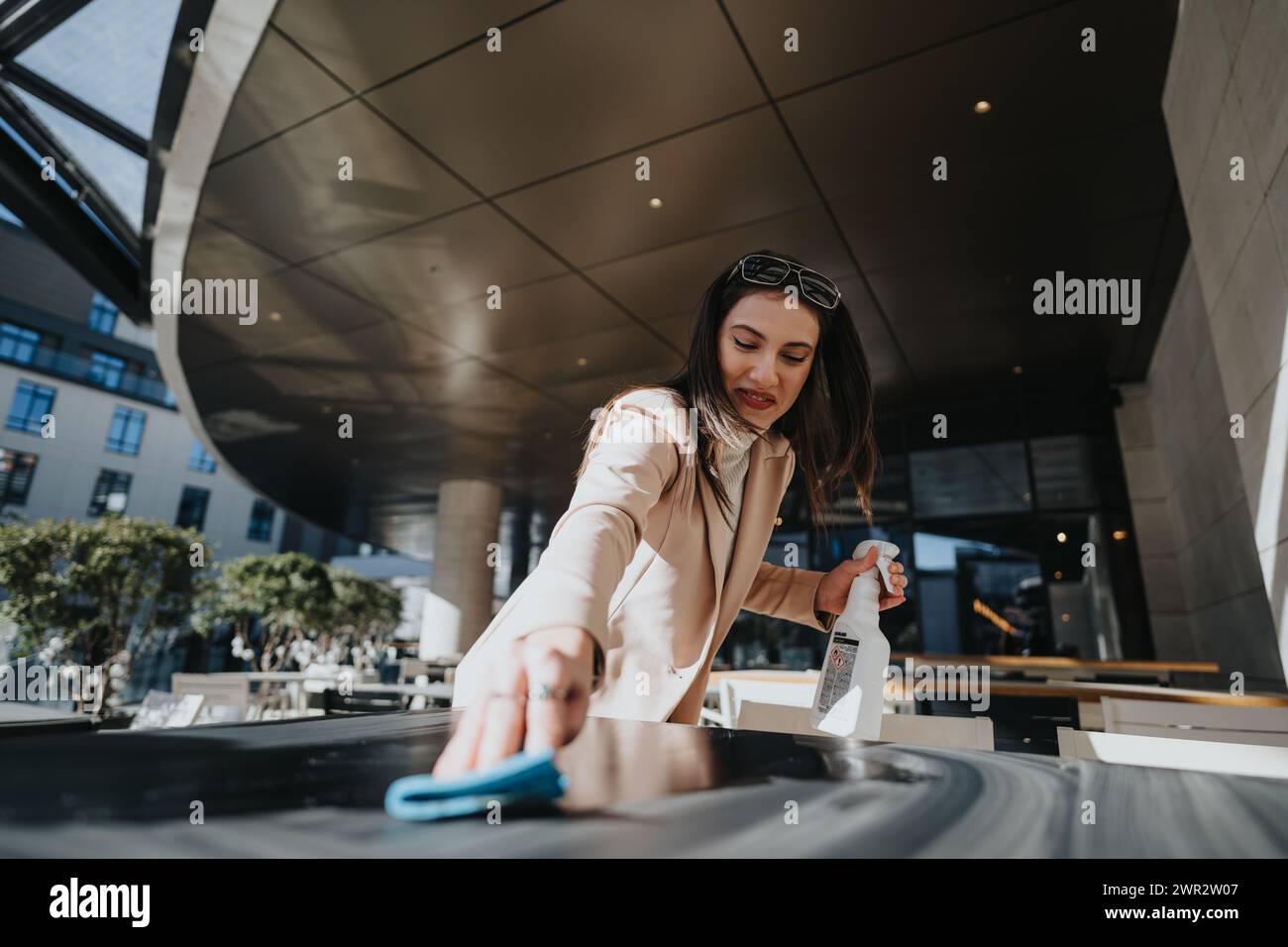 Diligent employee sanitizing outdoor seating area of a modern cafe with ...