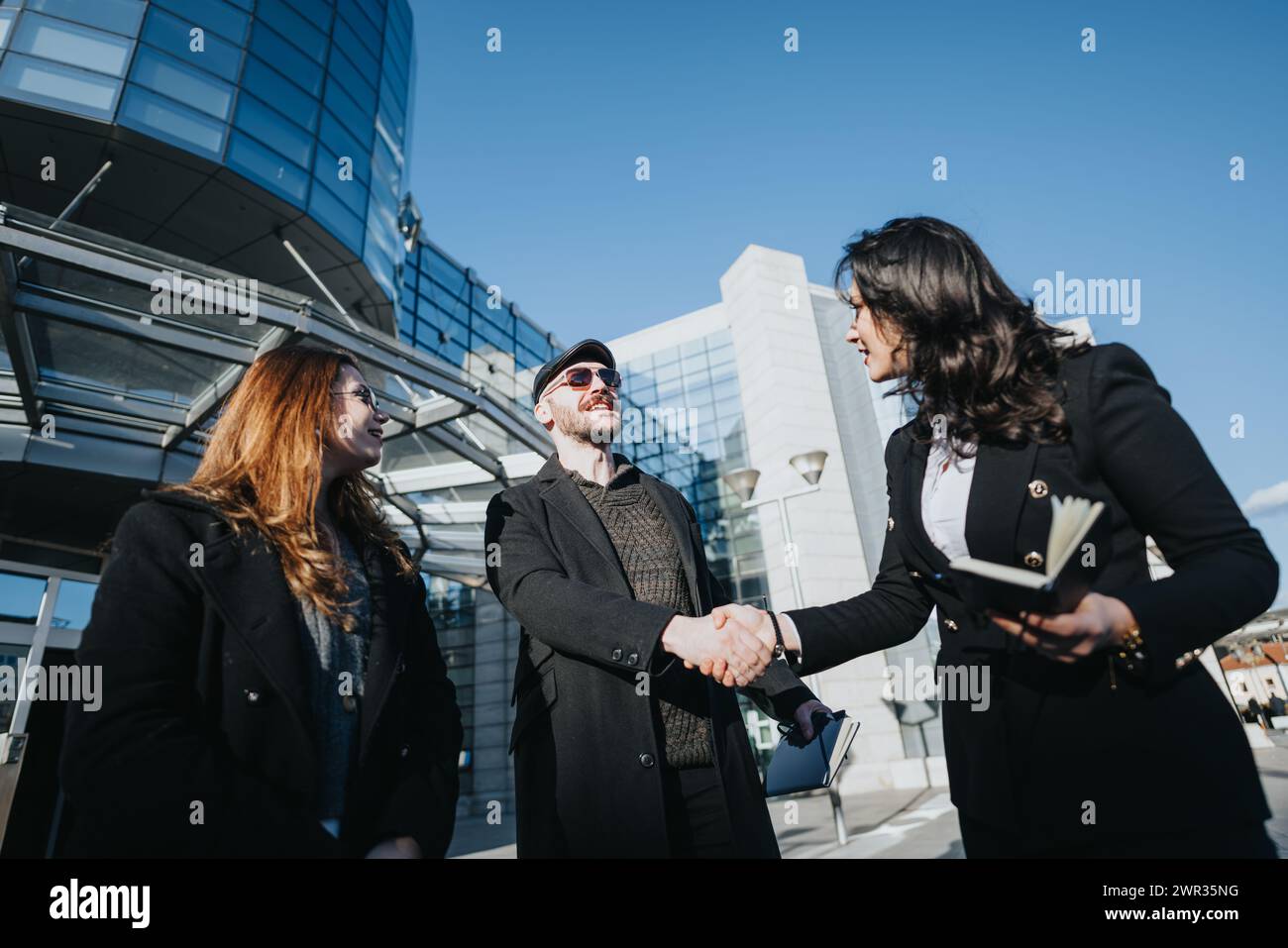 Three young professionals engage in a friendly handshake outside a ...