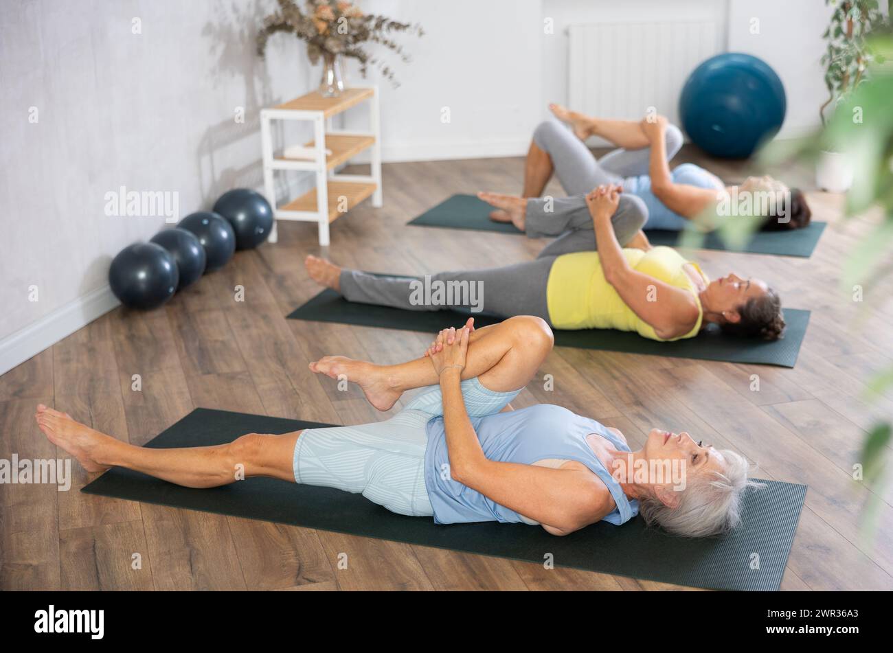 At yoga class elderly women is lying on back, bent one leg at knee and ...