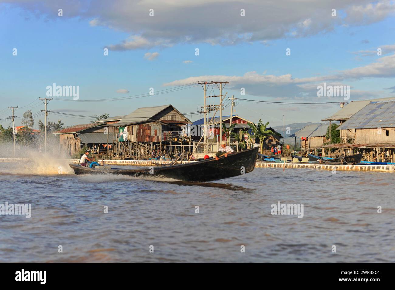 Fishing boat passes stilt houses of a waterfront village, Pindaya, Inle ...