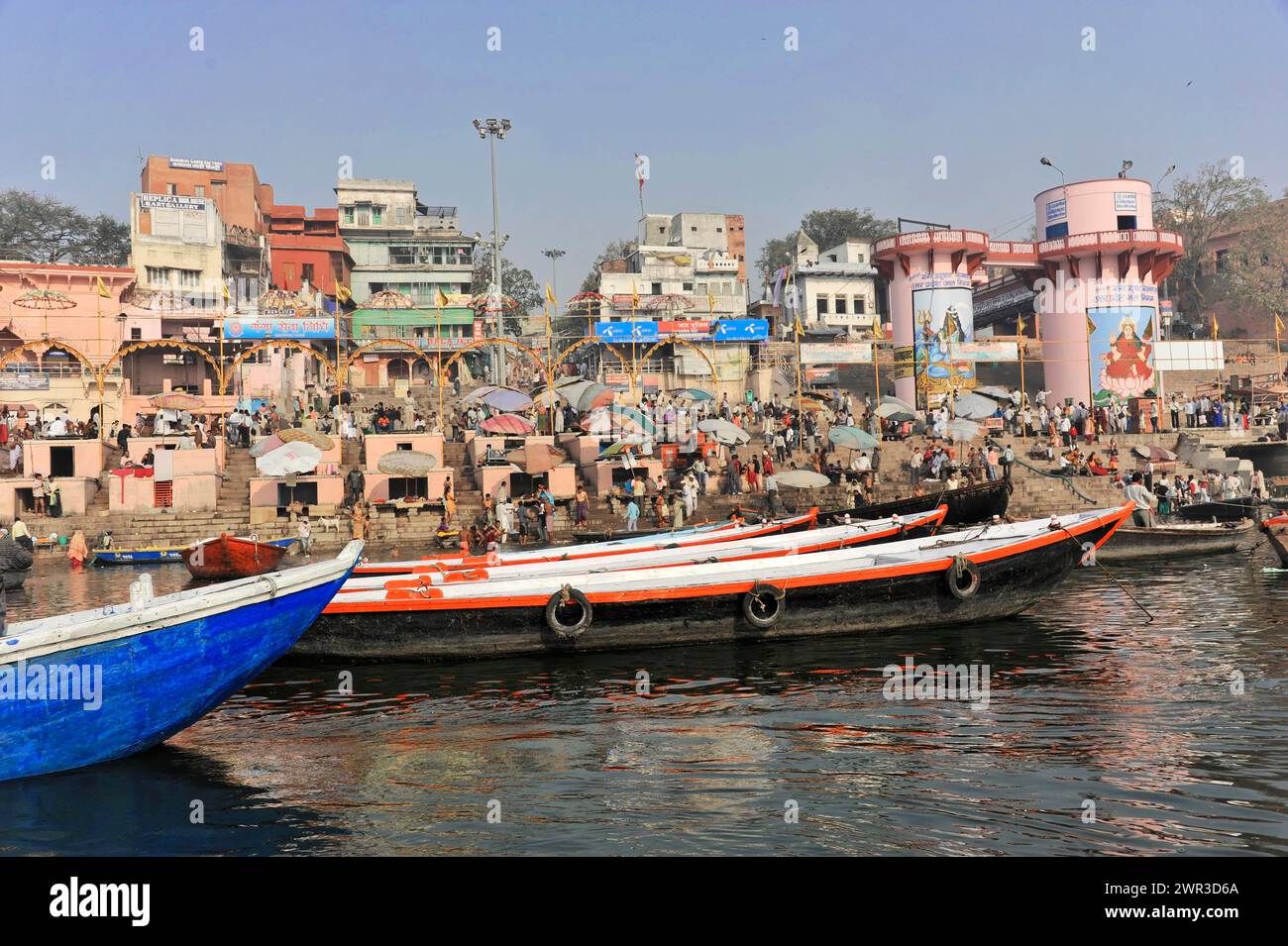 Colourful boats in front of a lively riverside town under a blue sky ...