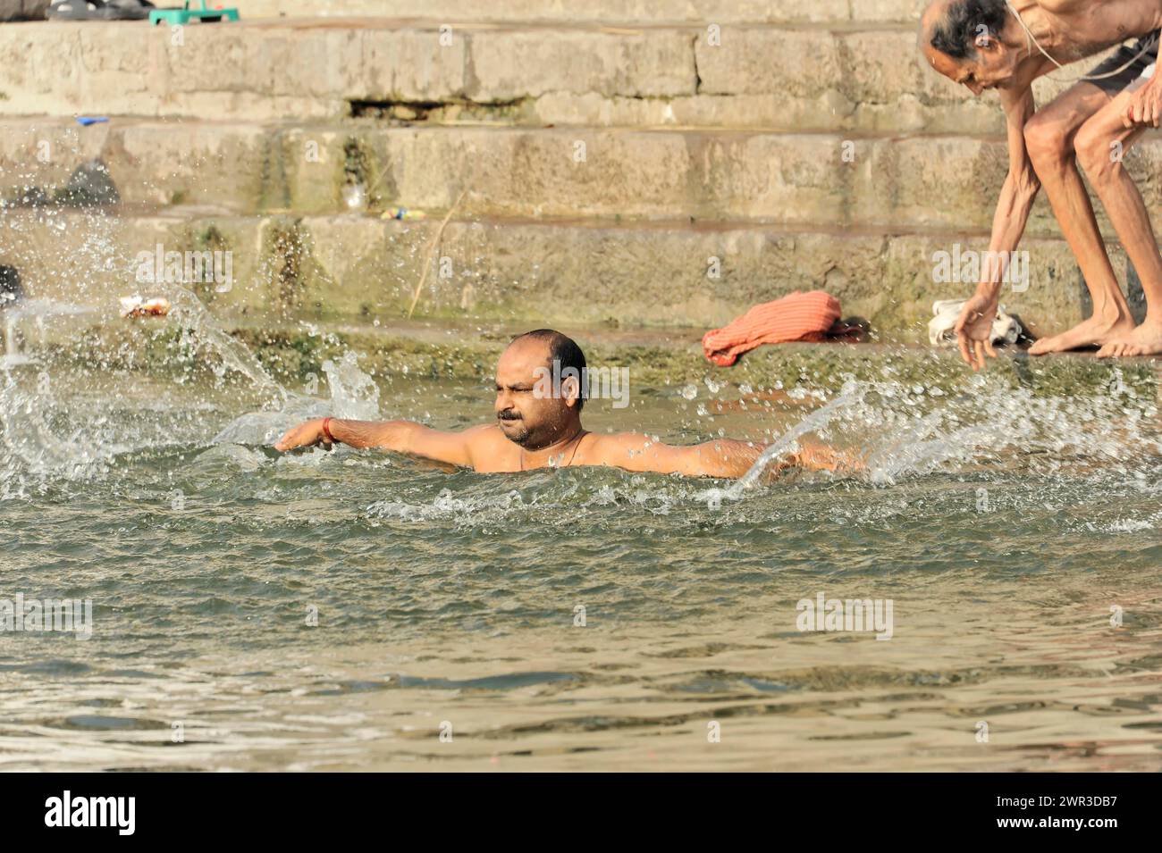 Two men bathing in the river, with water splashes around the swimmer ...
