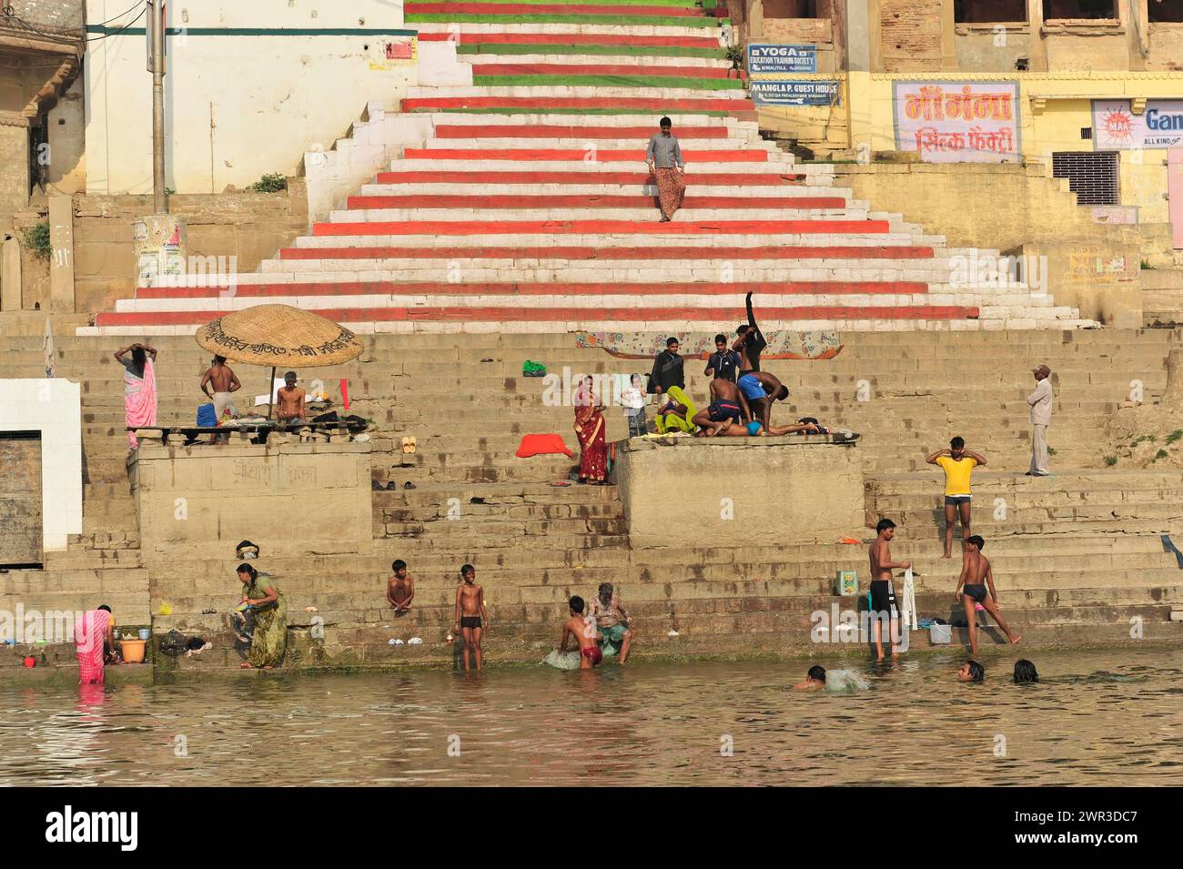 People on river steps, some bathing in the water, with a parasol in the ...