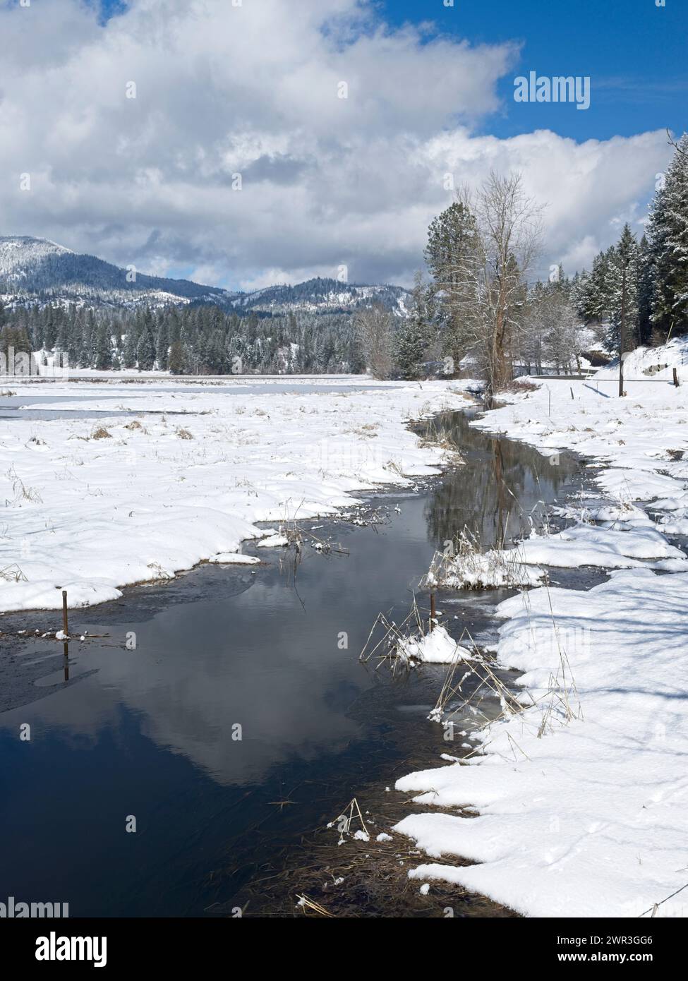 A small stream runs through a snow covered field in winter in north ...