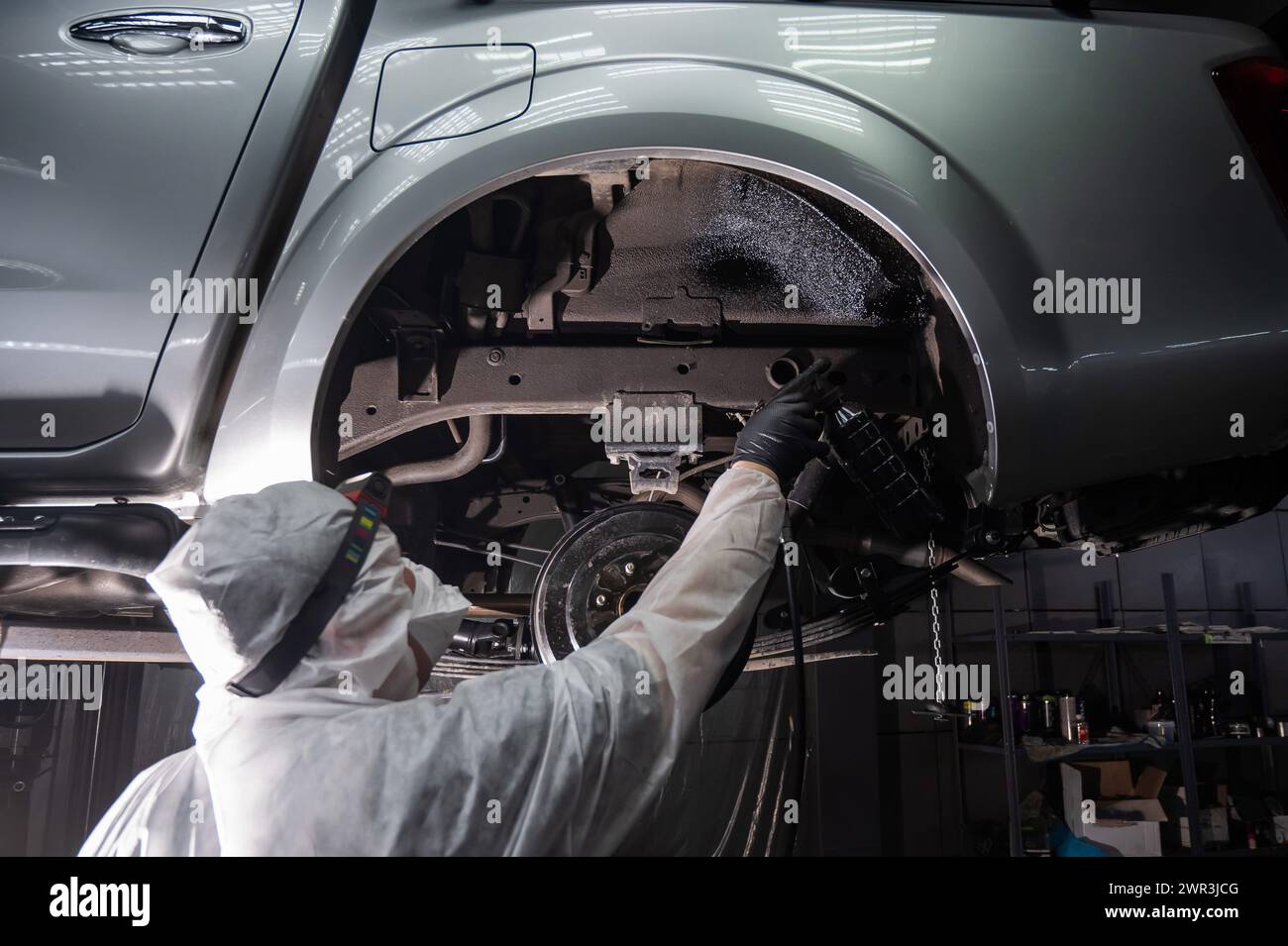 An auto mechanic applies anti-corrosion mastic to the underbody of a ...