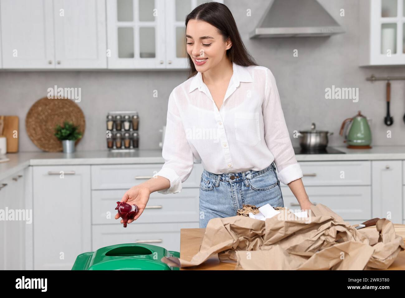 Garbage sorting. Smiling woman throwing onion peel into trash bin in ...