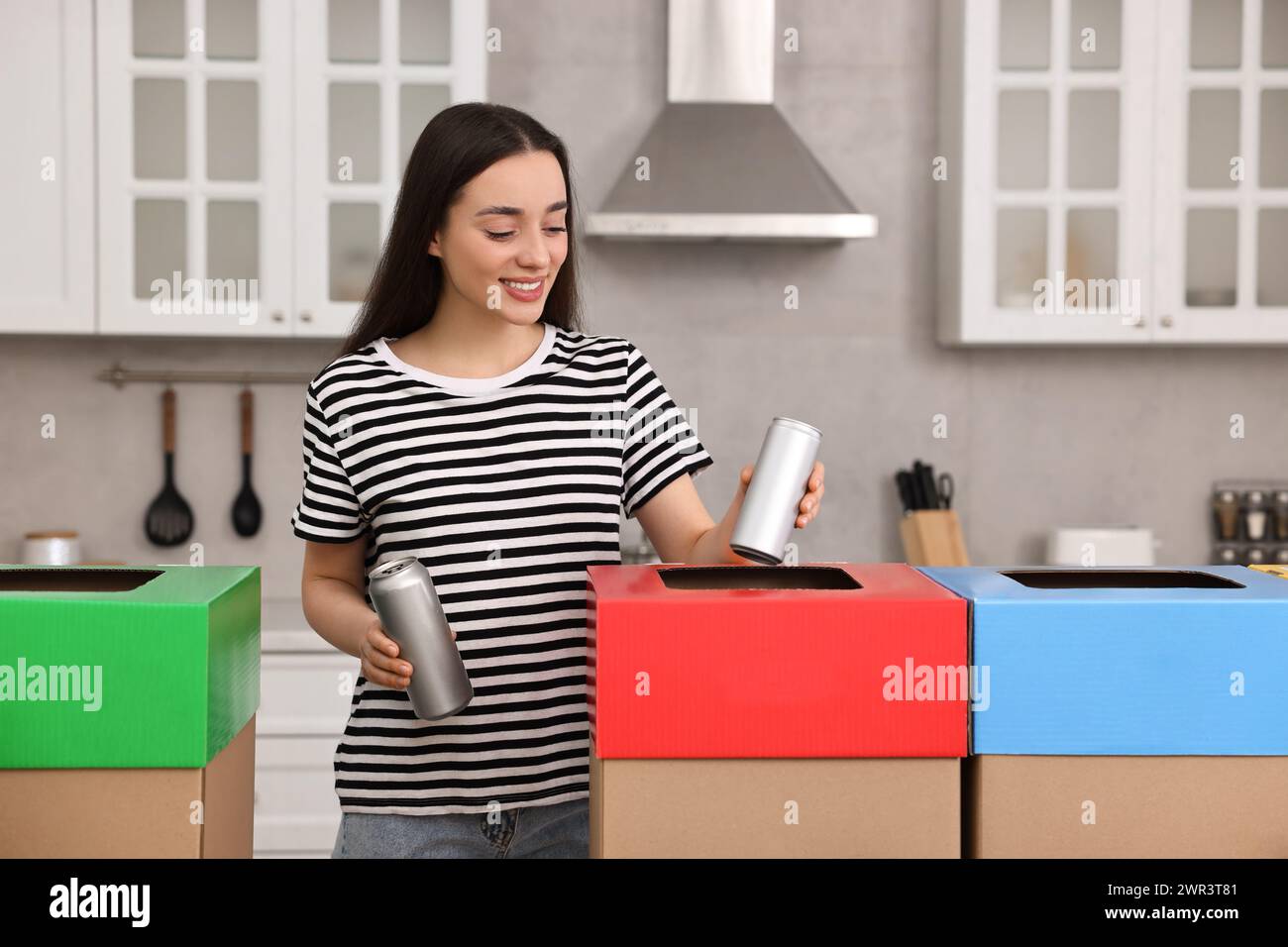 Garbage sorting. Smiling woman throwing metal can into cardboard box in ...
