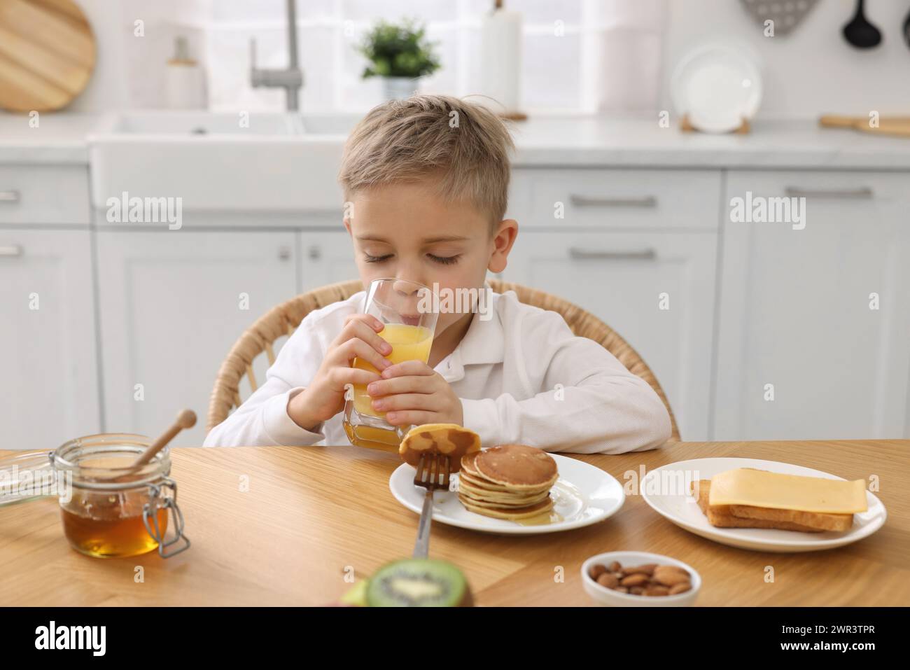 Breakfast time. Cute little boy drinking juice at table in kitchen ...