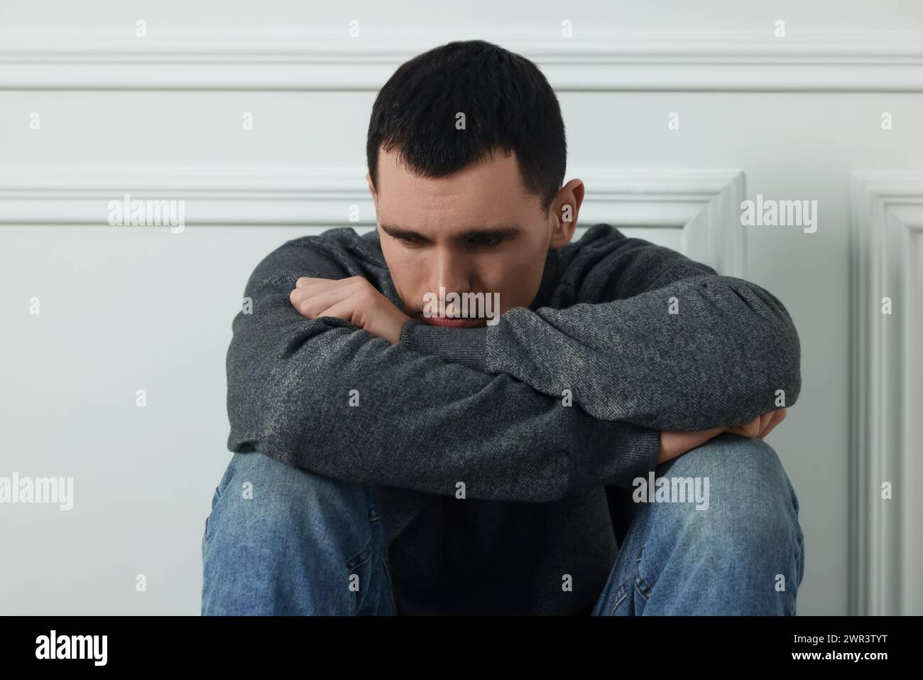 Sad man sitting near white wall indoors Stock Photo - Alamy