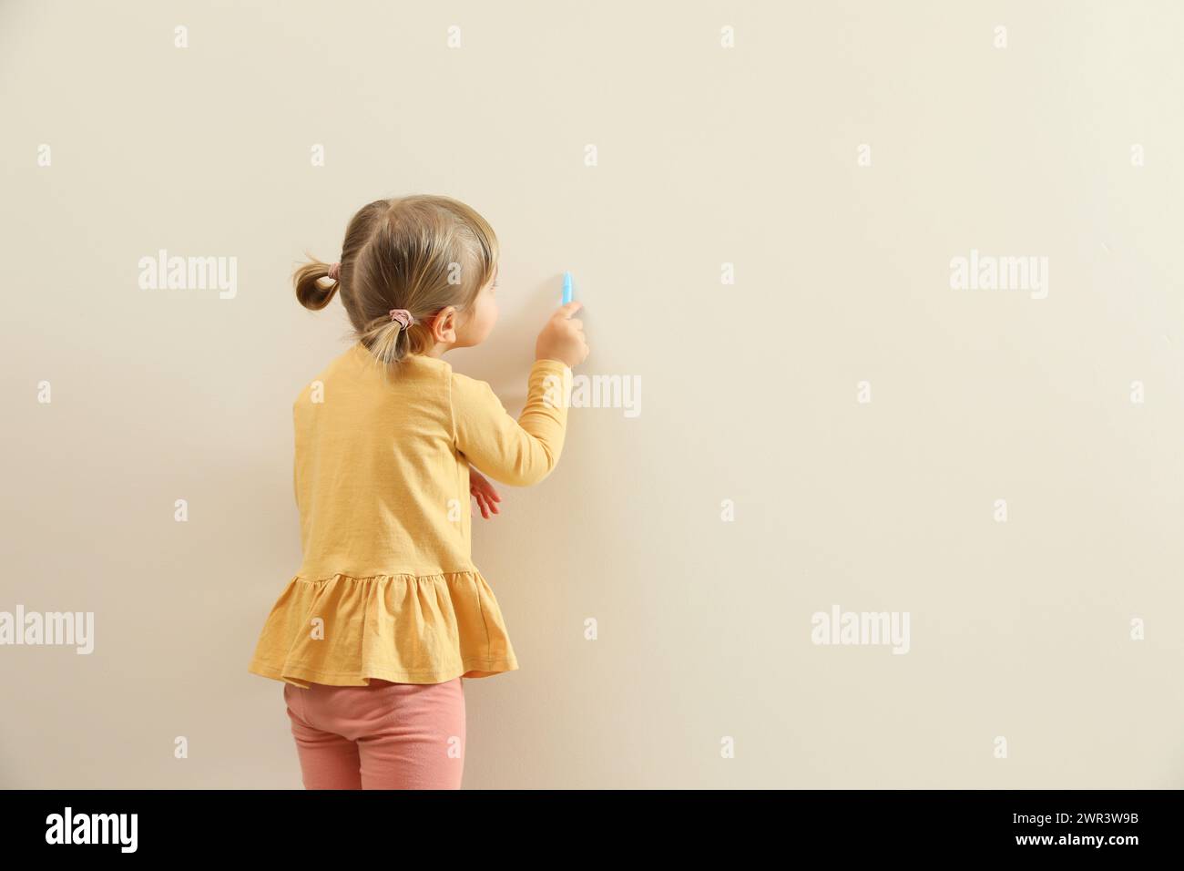 Little girl drawing on beige wall, back view and space for text. Child ...