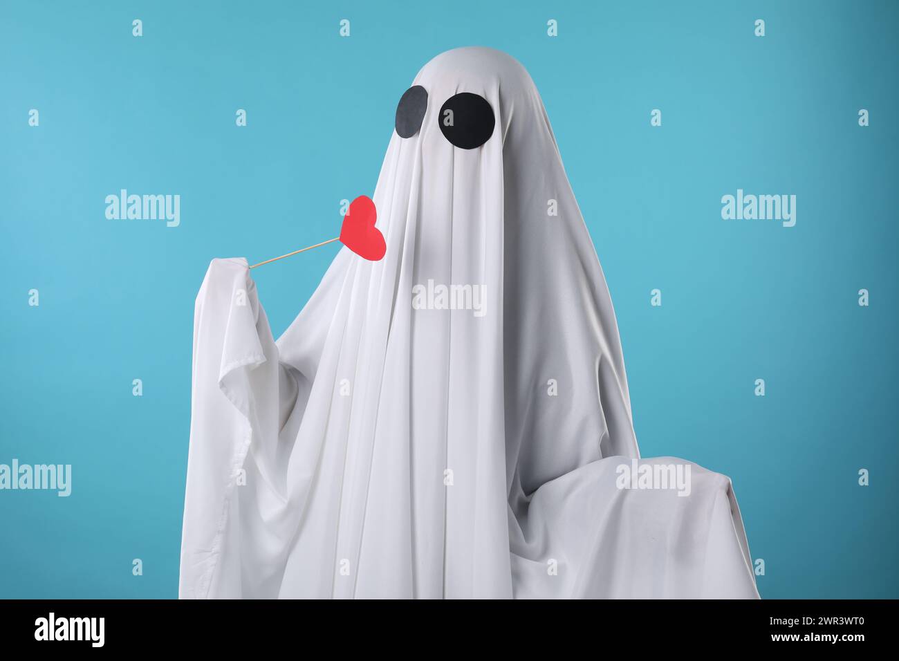 Cute ghost. Person covered with white sheet holding stick with red ...