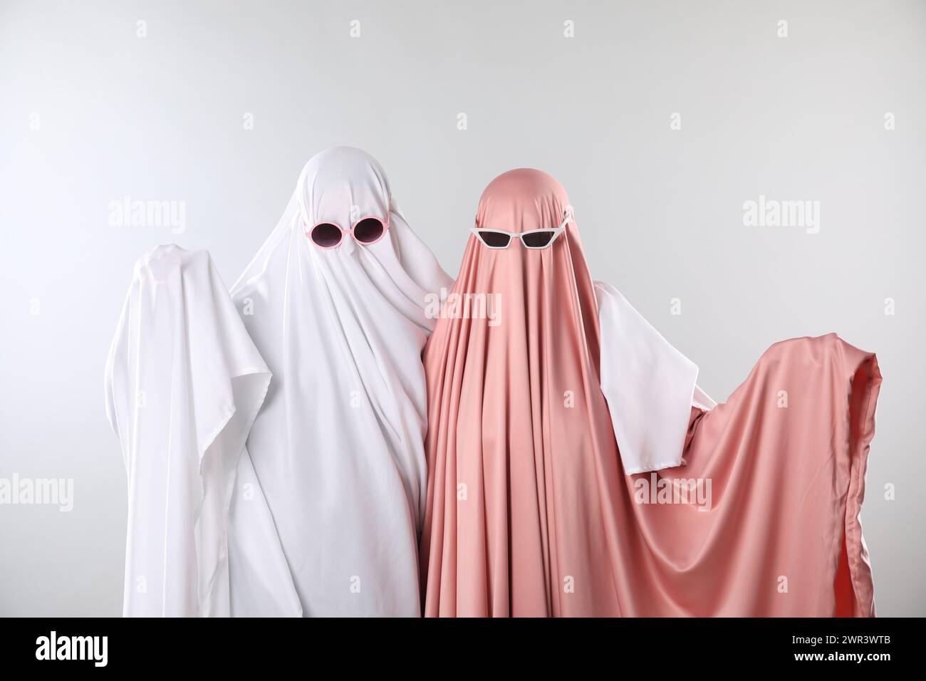 Glamorous ghosts. Women in color sheets with sunglasses on light grey ...