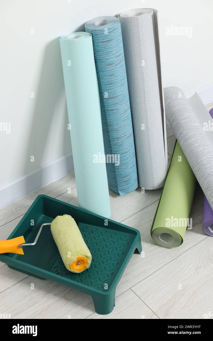 Different wallpaper rolls, roller and tray near white wall indoors ...