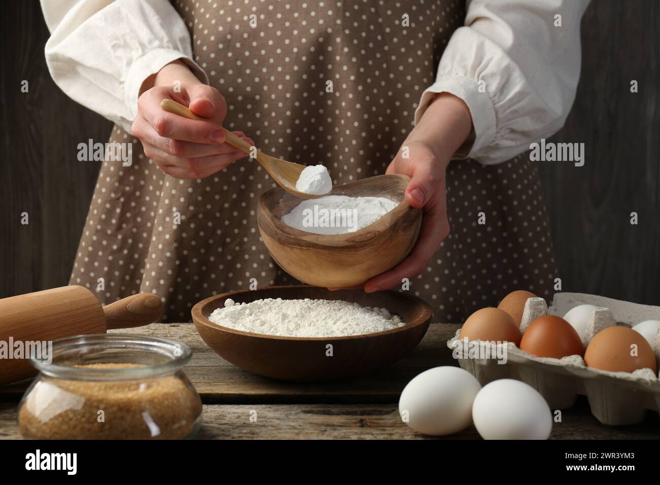 Making dough. Woman adding baking powder to flour at wooden table ...