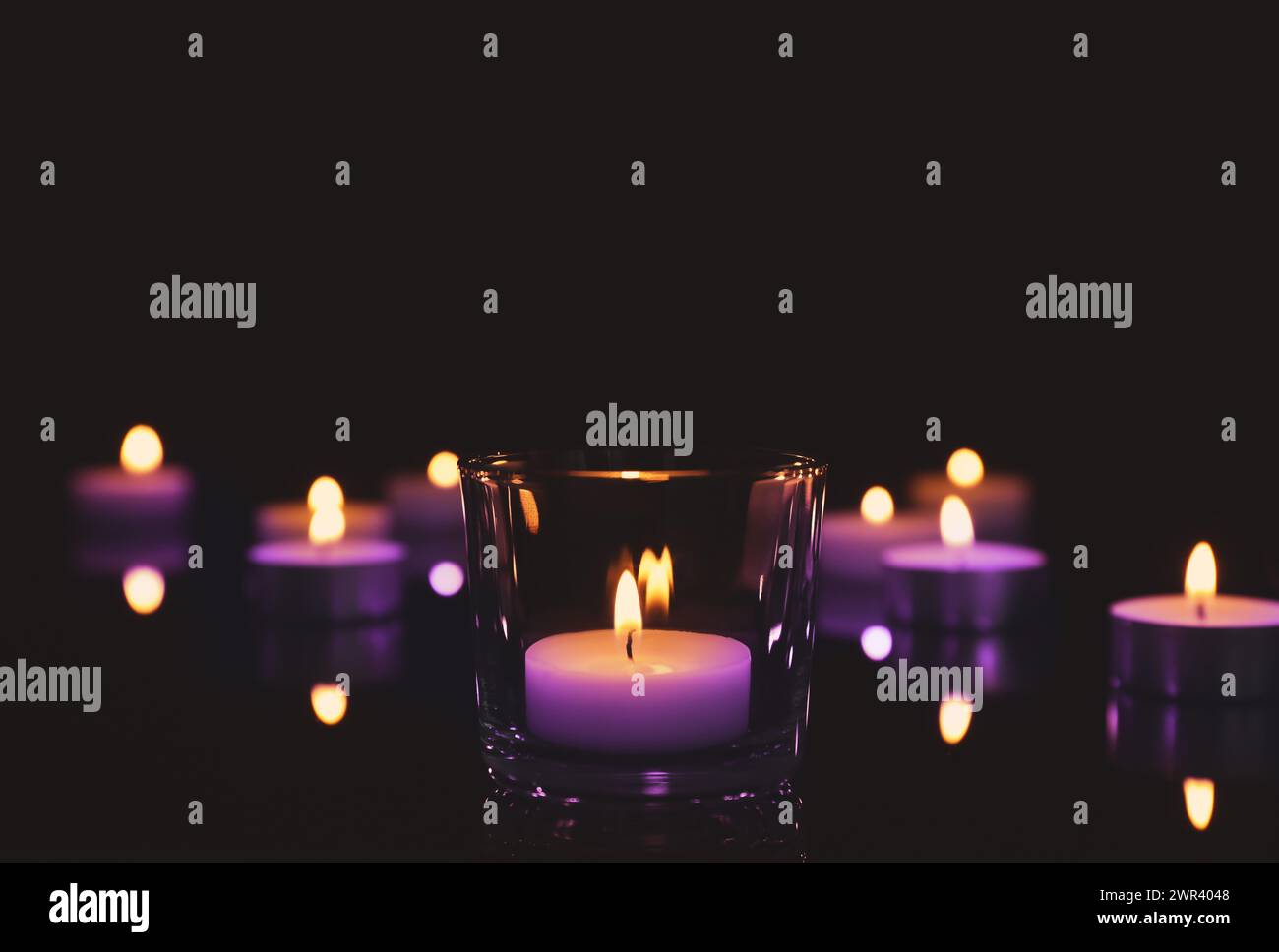 Beautiful burning violet wax candles on black background. Funeral ...
