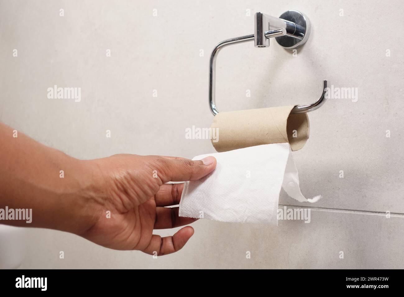 Hand pulling toilet paper roll in holder Stock Photo - Alamy