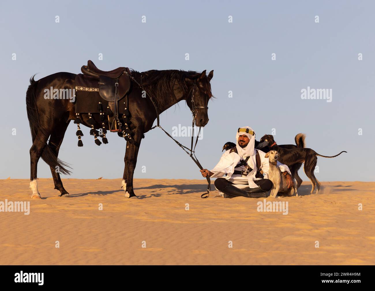 Man in traditional Saudi Arabian clothing in a desert with a black ...