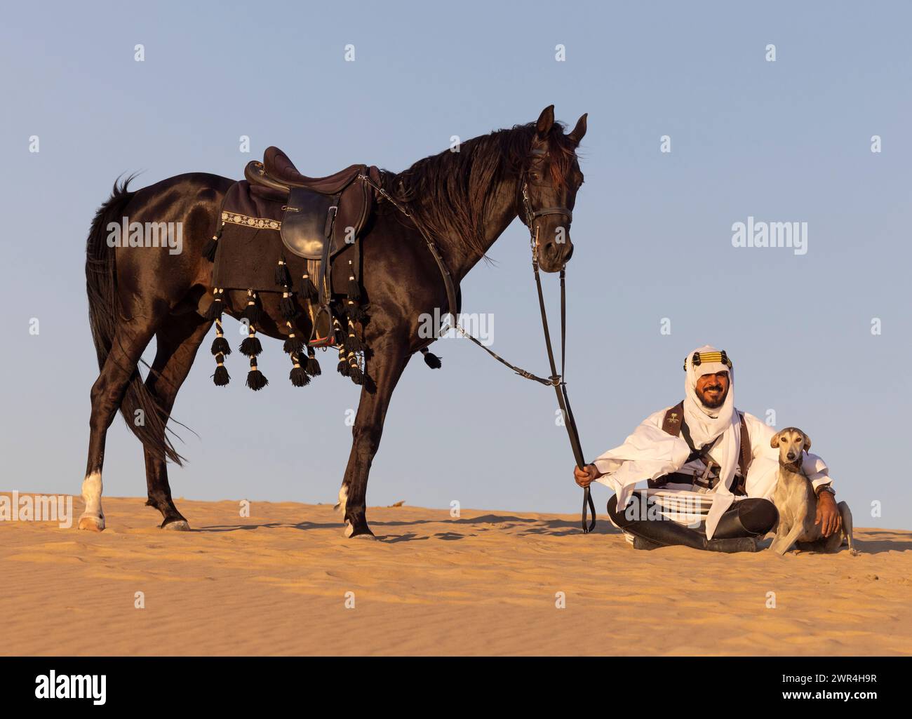Man in traditional Saudi Arabian clothing in a desert with a black ...
