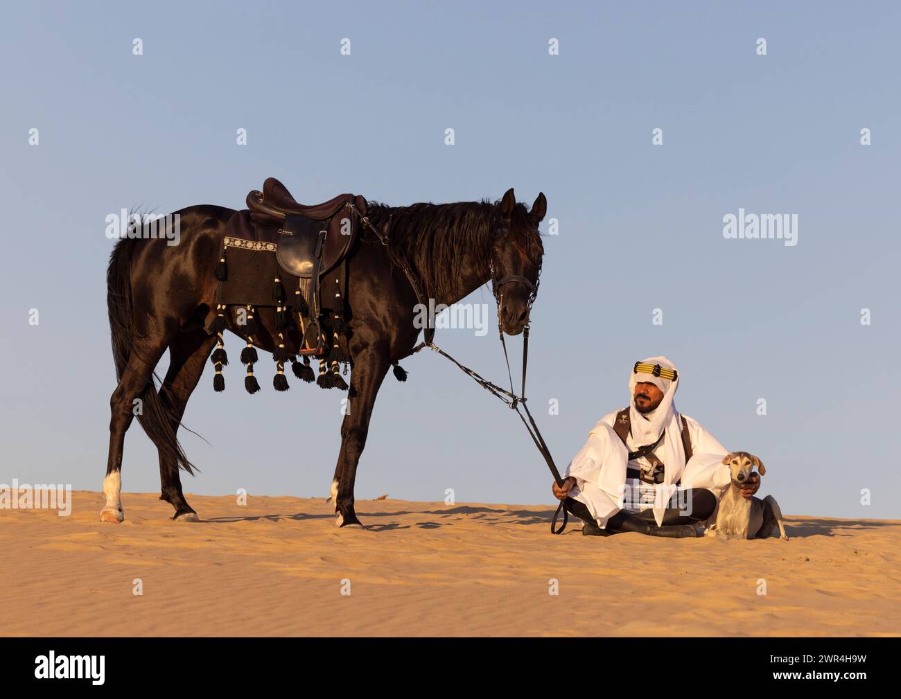 Man in traditional Saudi Arabian clothing in a desert with a black ...