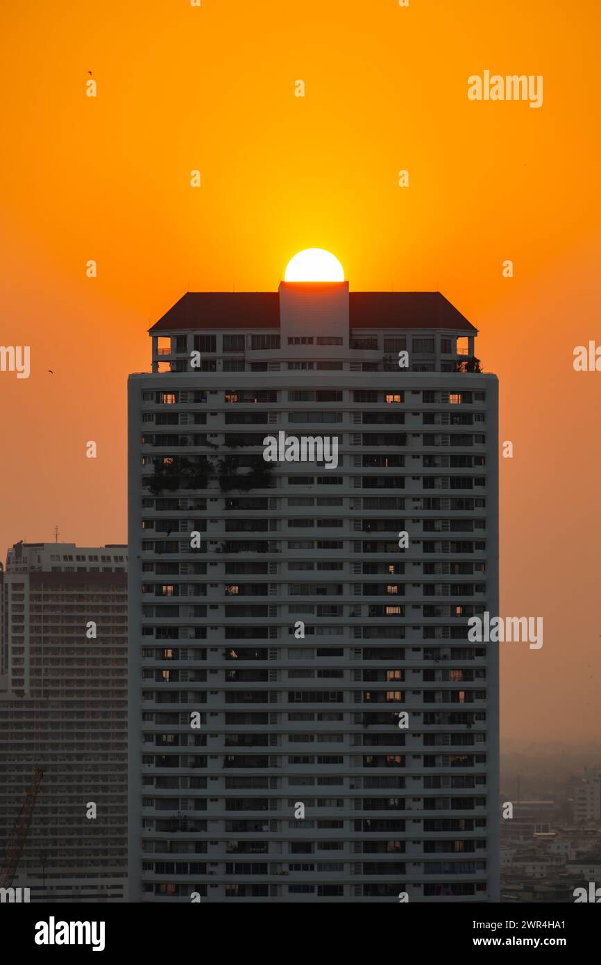 As the sun sets over Bangkok half of it is visible just on top of a ...