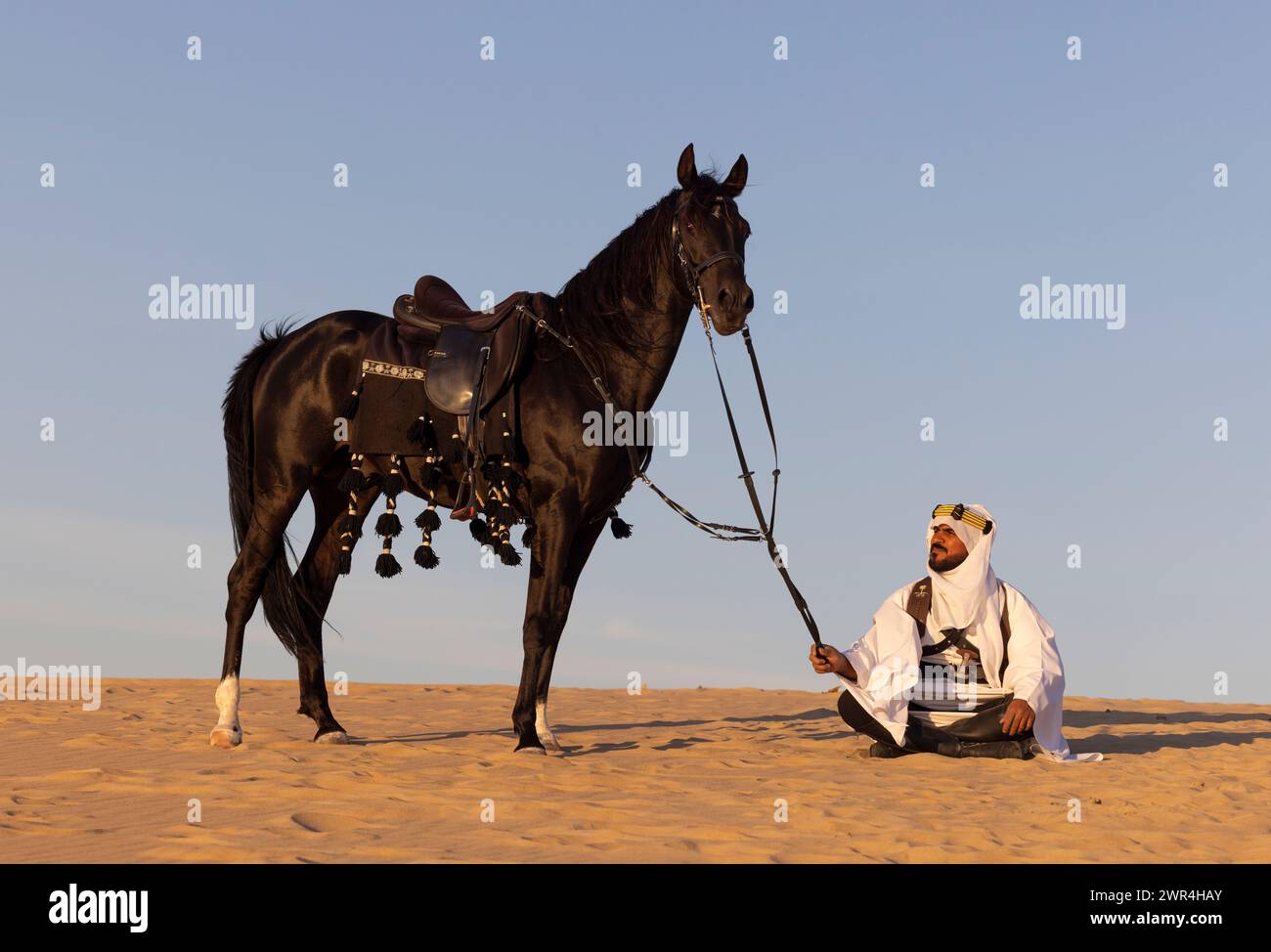 Man in traditional Saudi Arabian clothing in a desert with a black ...