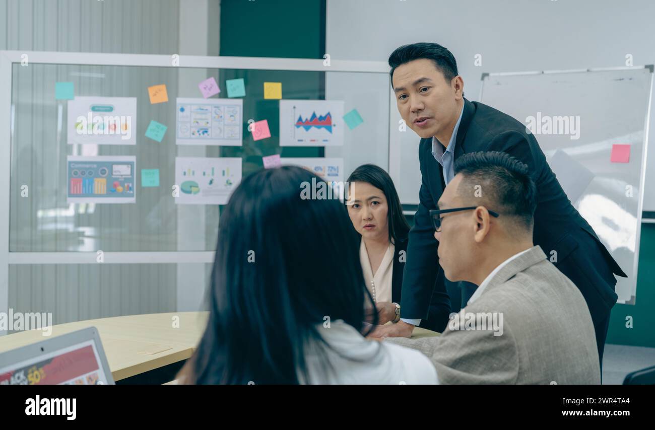 A group of people are gathered around a table with a whiteboard behind ...