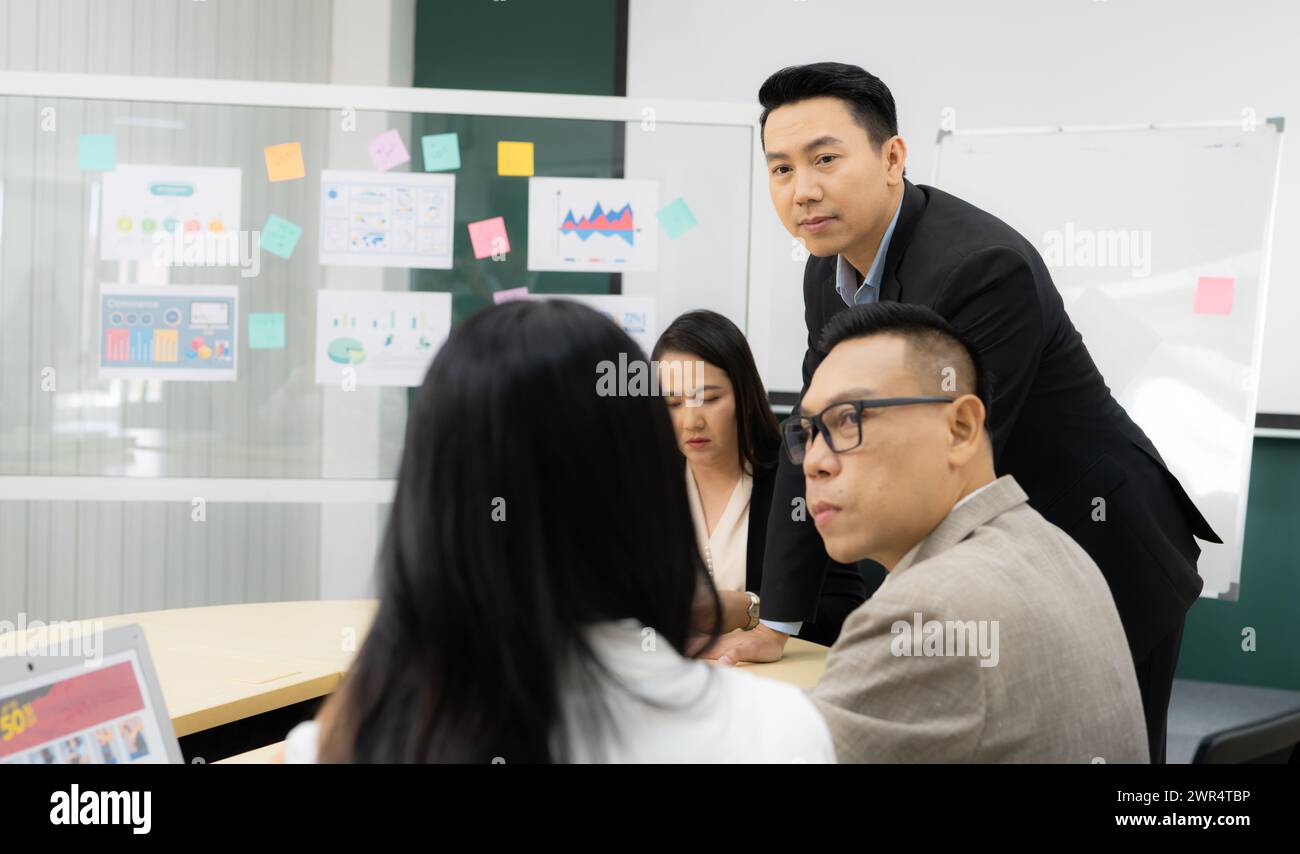 A group of people are gathered around a table with a whiteboard behind ...