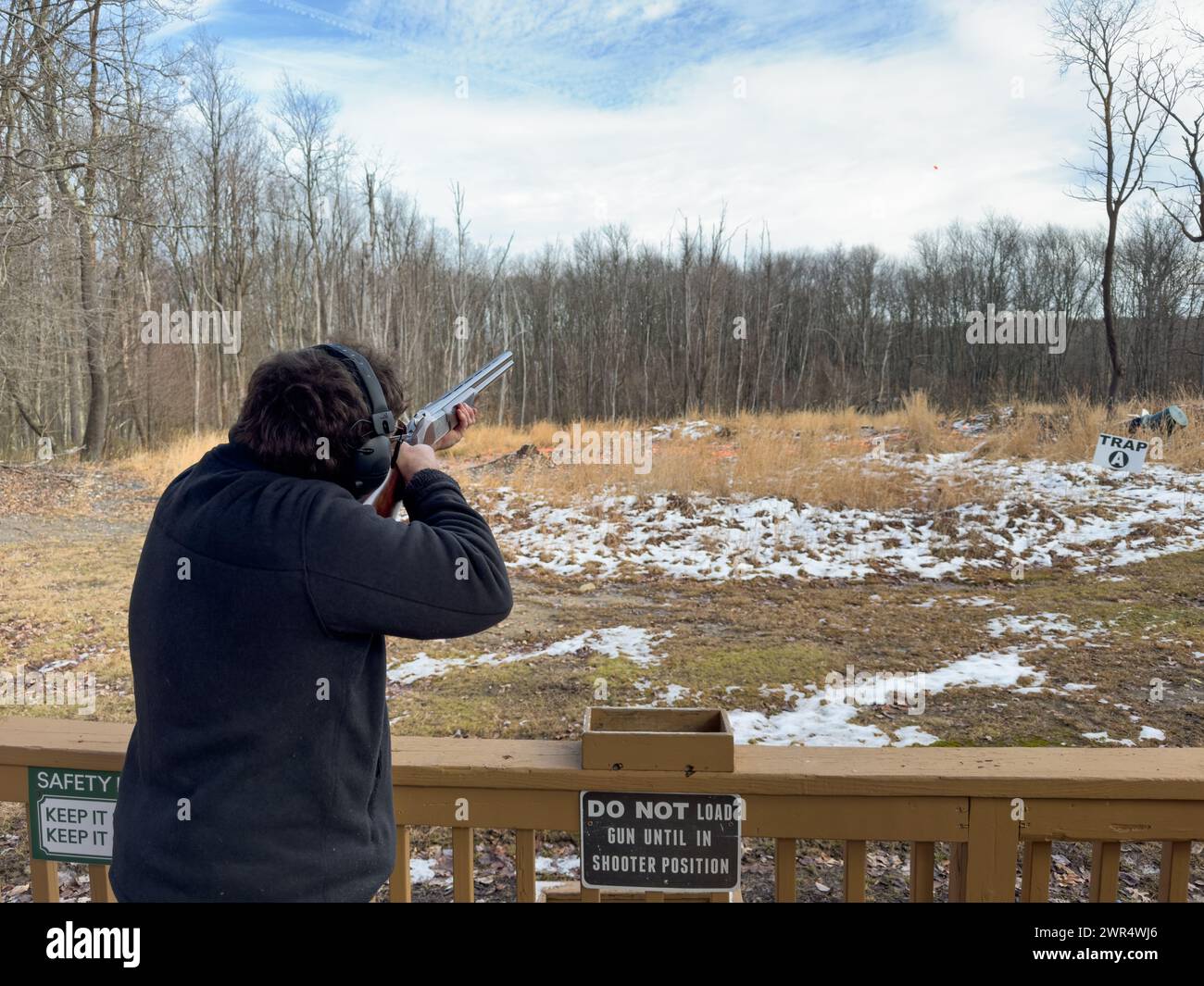 A young man shooting sporting clays with a shotgun at a shooting range ...