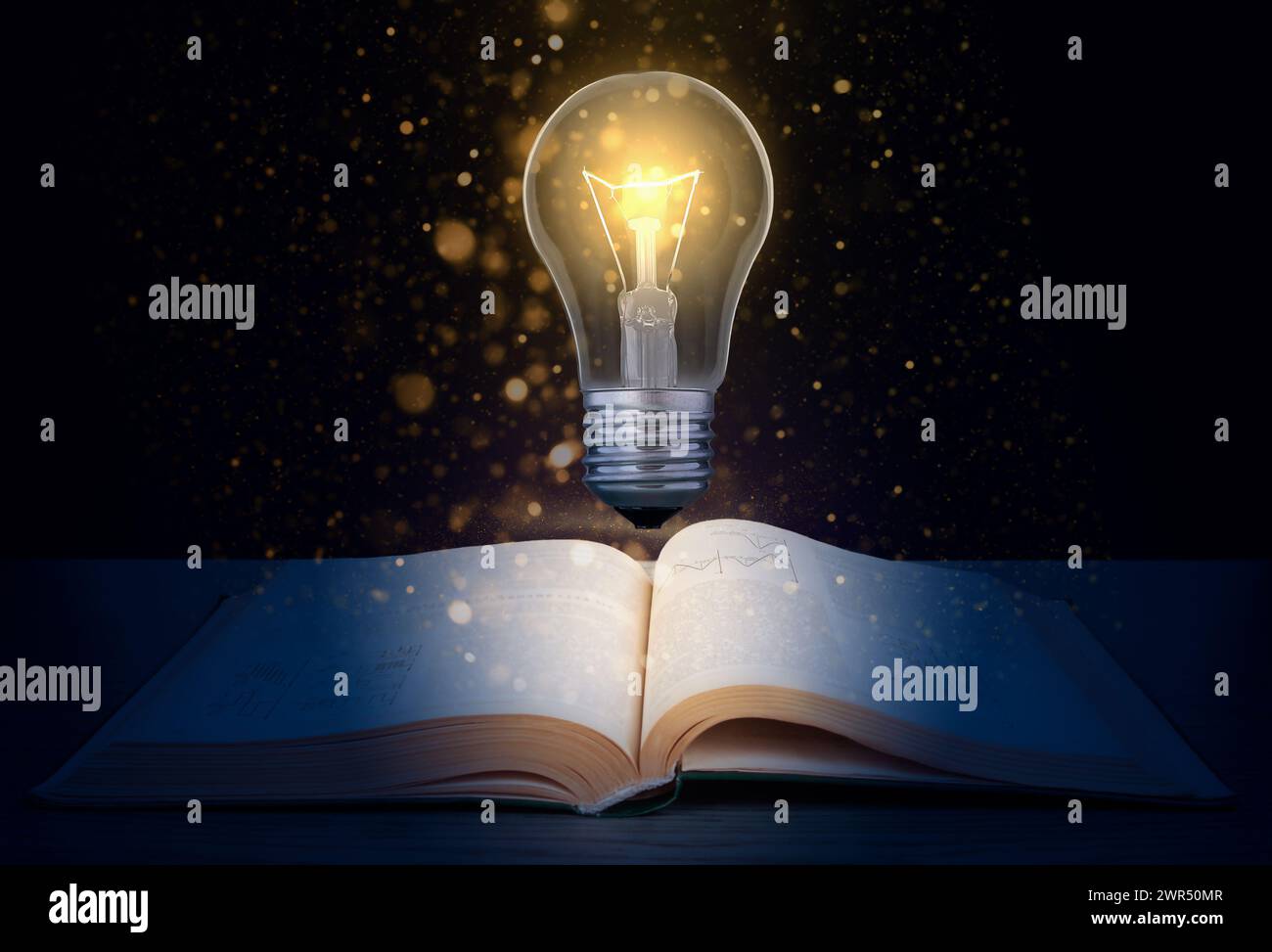 Glowing light bulb over a textbook on a dark background with glitter. Concept to produce a new ...