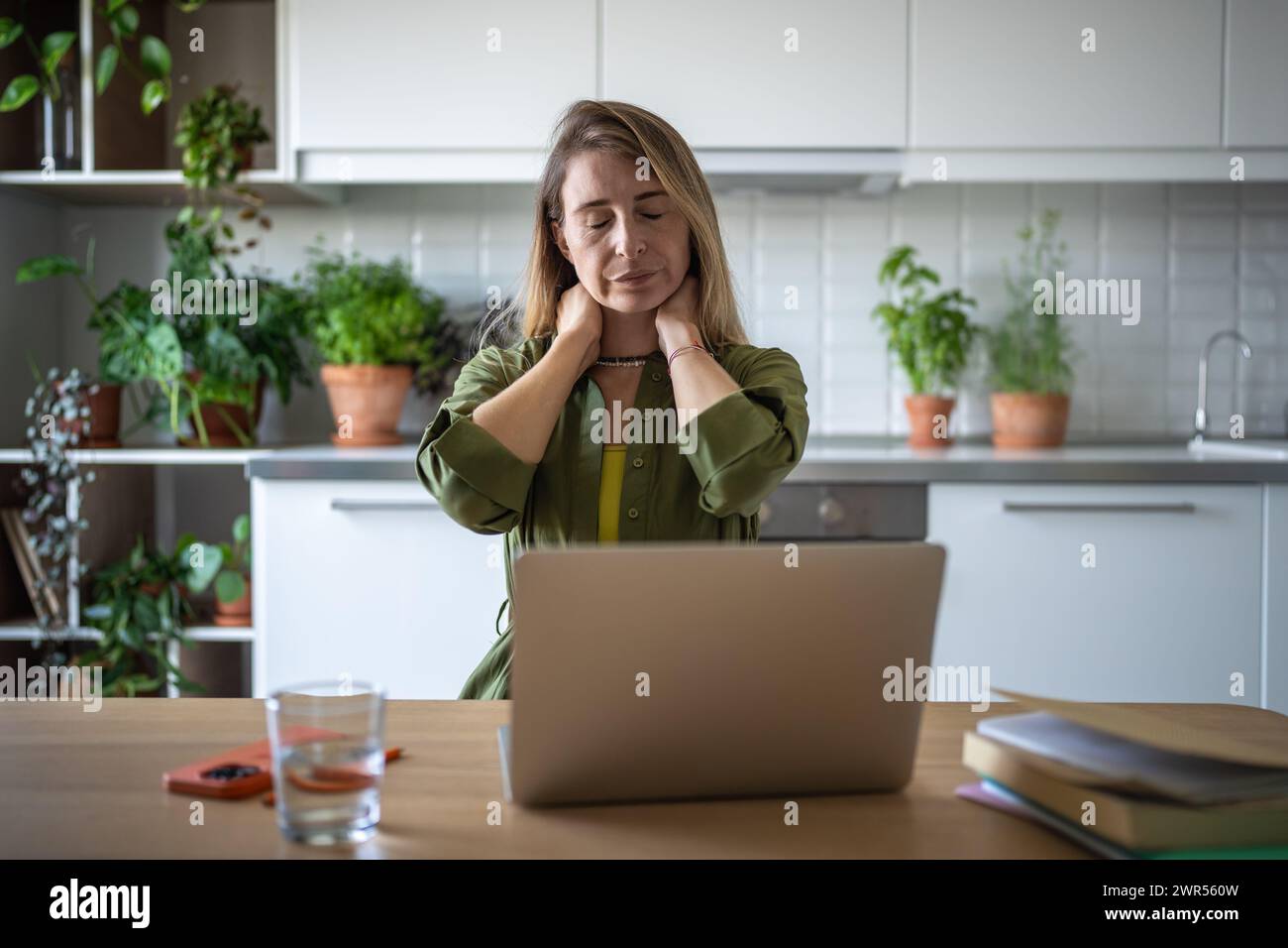 Tired unwell freelance woman sit at table with laptop holding neck with ...