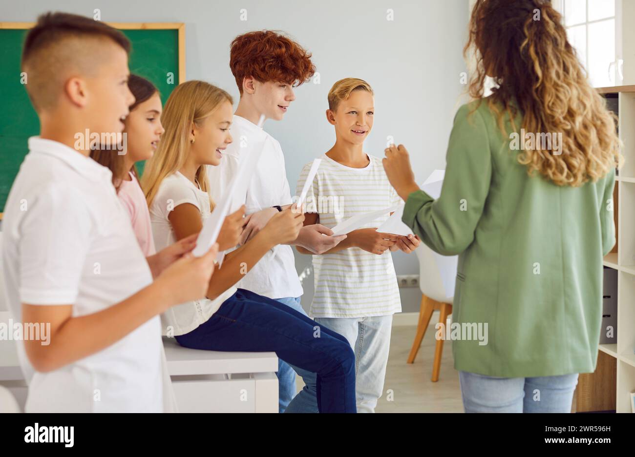 School children in classroom with teacher singing in choir during music ...