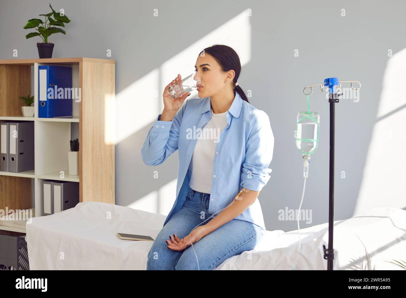 Woman drinking water while receiving vitamin solution infusion through ...