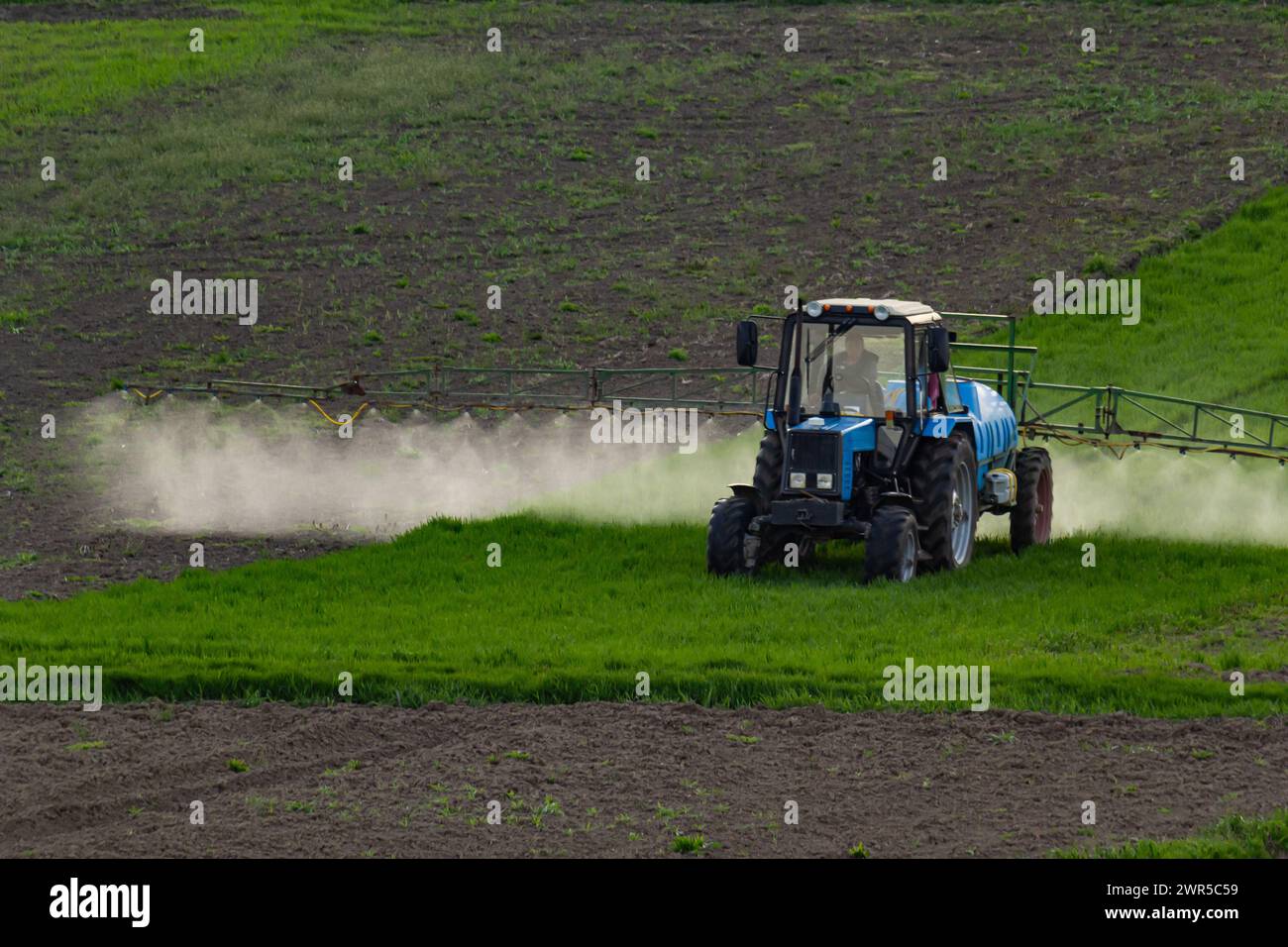 Aerial view of tractor spraying crop in green farm fields with ...