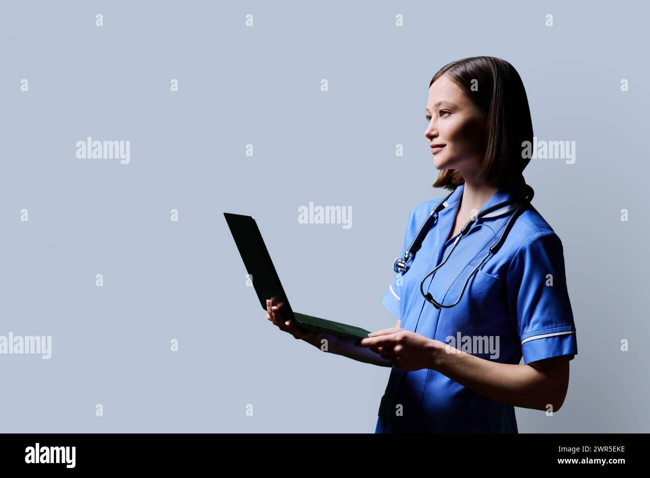 Female nurse using laptop, profile view on gray studio background Stock ...