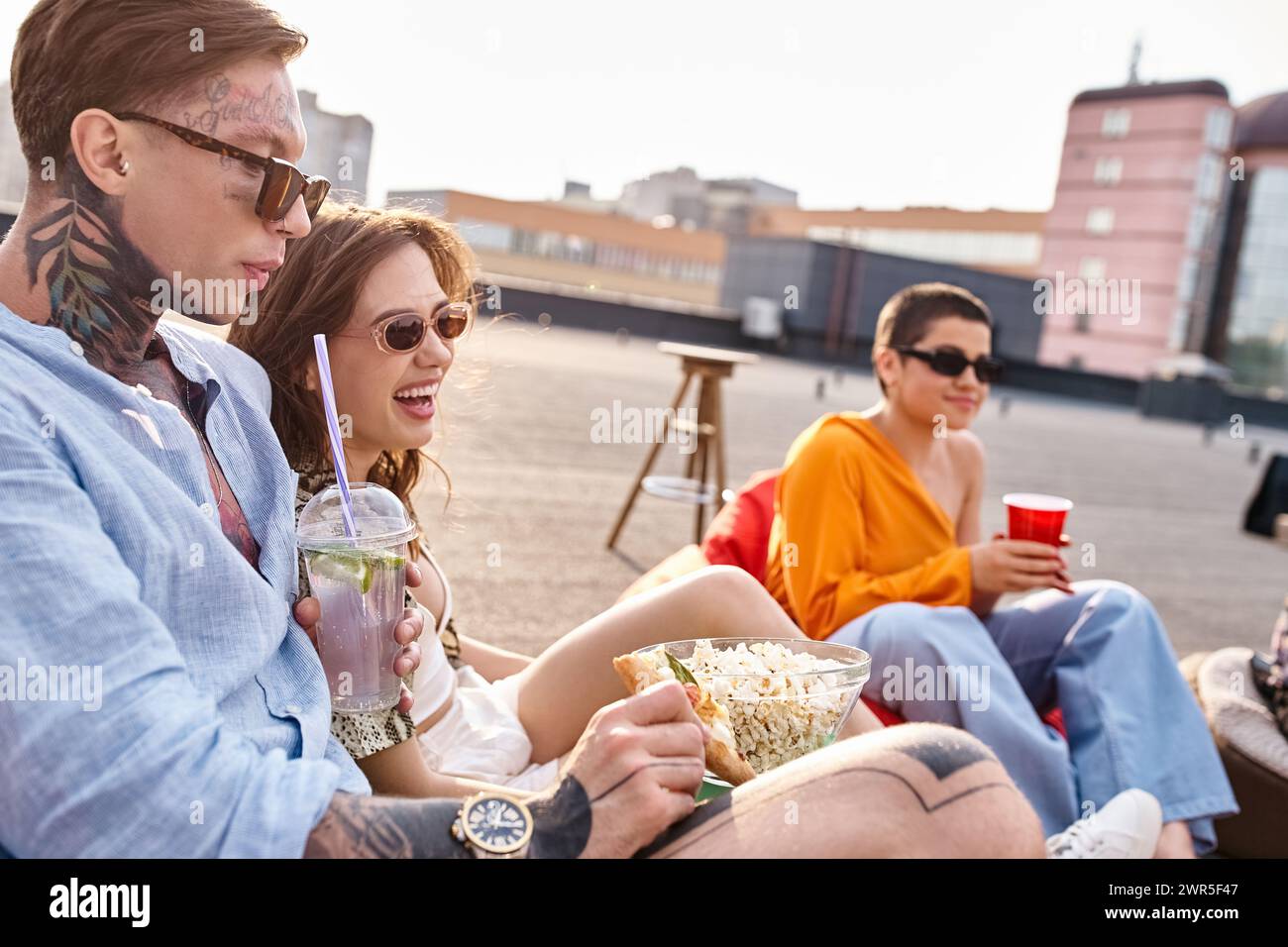good looking jolly friends in urban attires sitting on rooftop eating ...