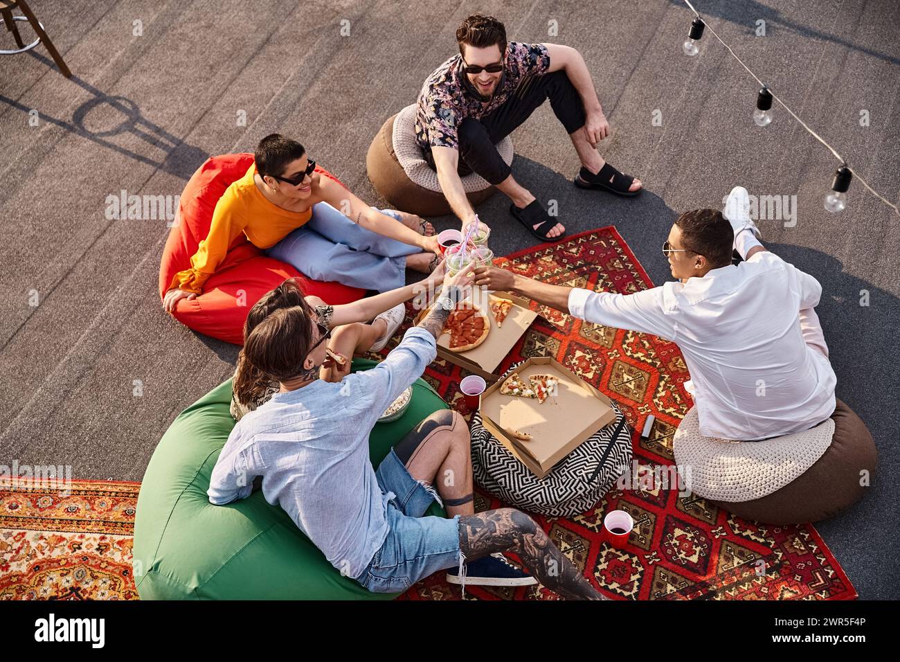 top view of five diverse jolly friends enjoying pizza and clinking cups ...