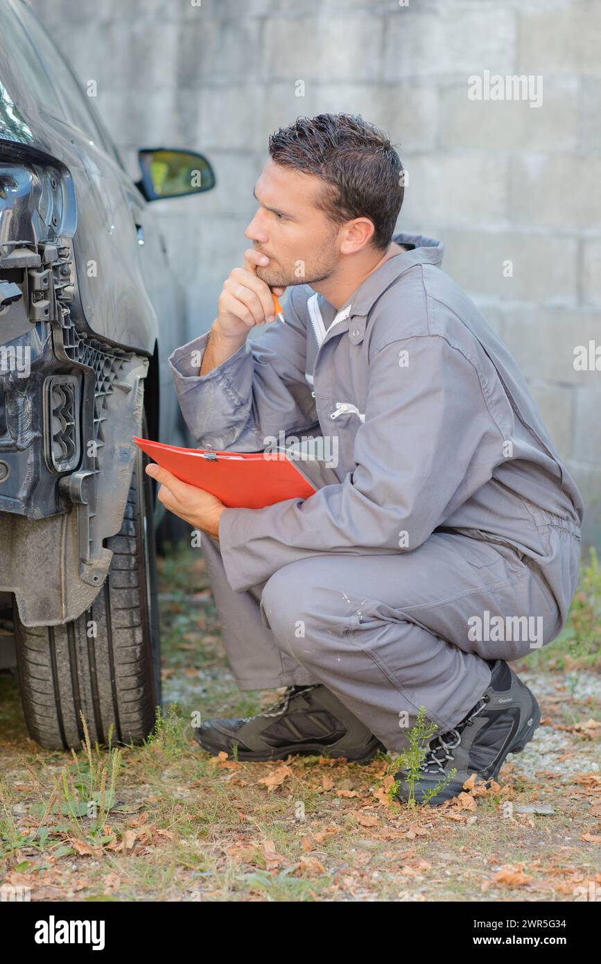 Mechanic holding clipboard assessing accident damaged car Stock Photo ...