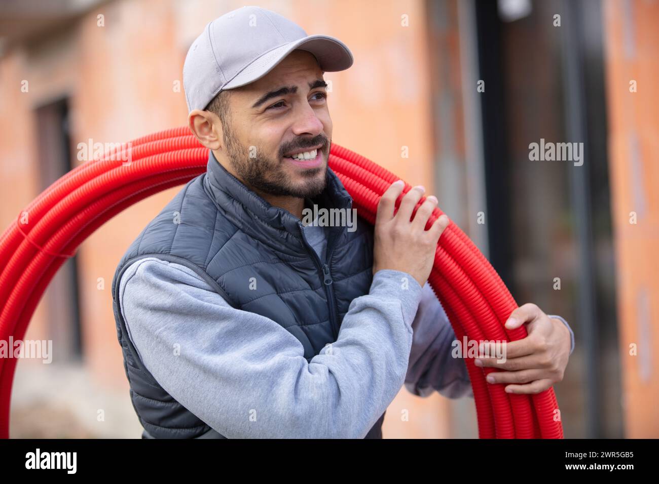 male builder carrying reel of red pipe on shoulder Stock Photo - Alamy