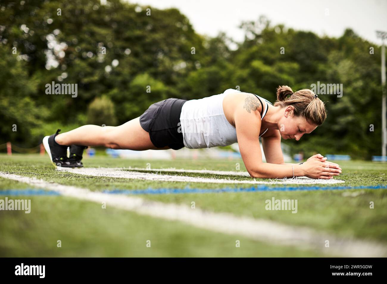 Female athlete doing plank exercise on athletic field, Lincoln ...