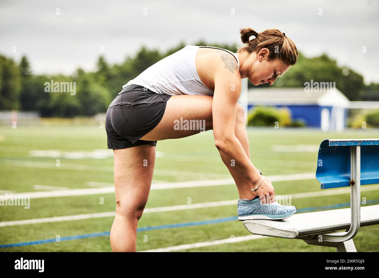 Female athlete tying sports shoe on bench at athletic field, Lincoln ...