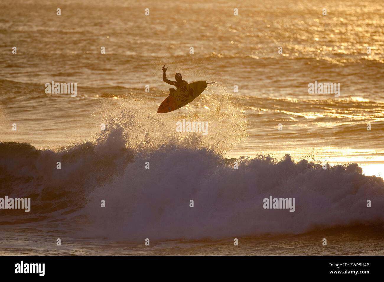 A surfer performing an aerial maneuver against the golden sunlight on ...