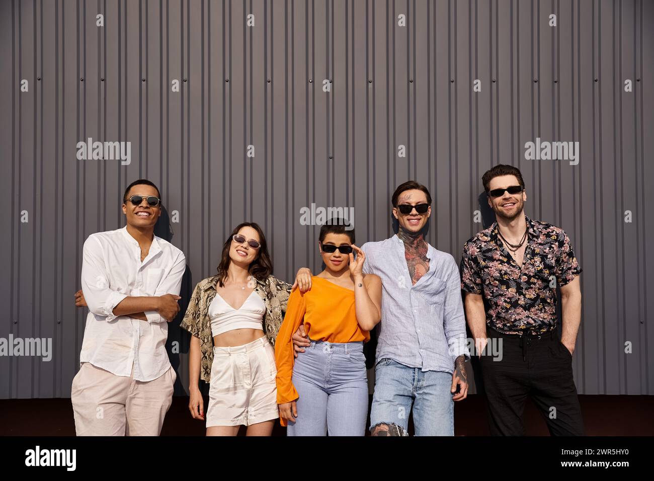 five multiracial joyful friends in vibrant outfits posing by wall and ...