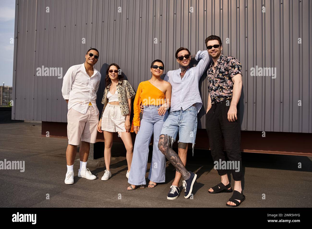 group of joyous multicultural friends in vibrant clothes posing by wall ...