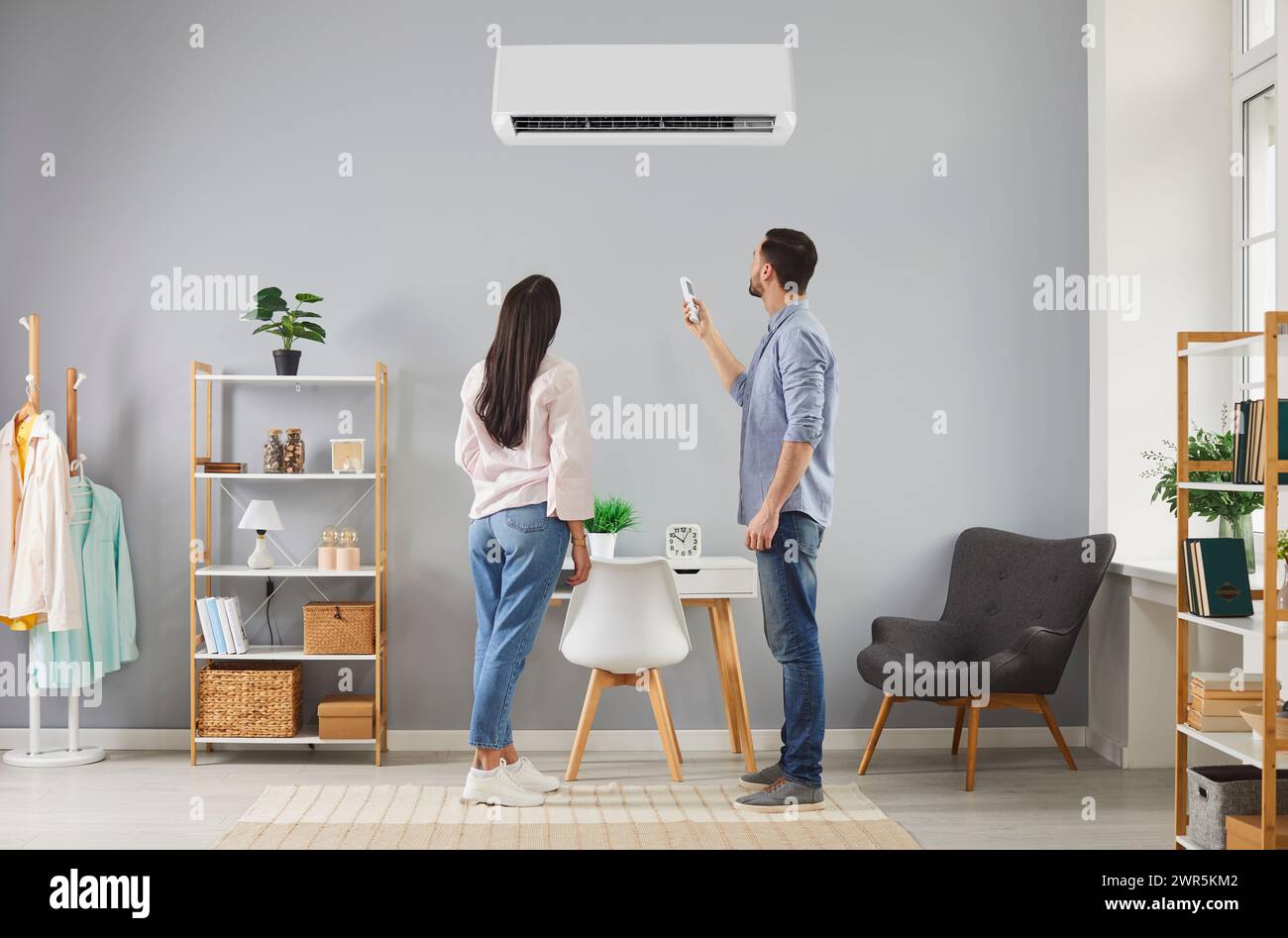 Young family couple setting up temperature on modern air conditioner in ...