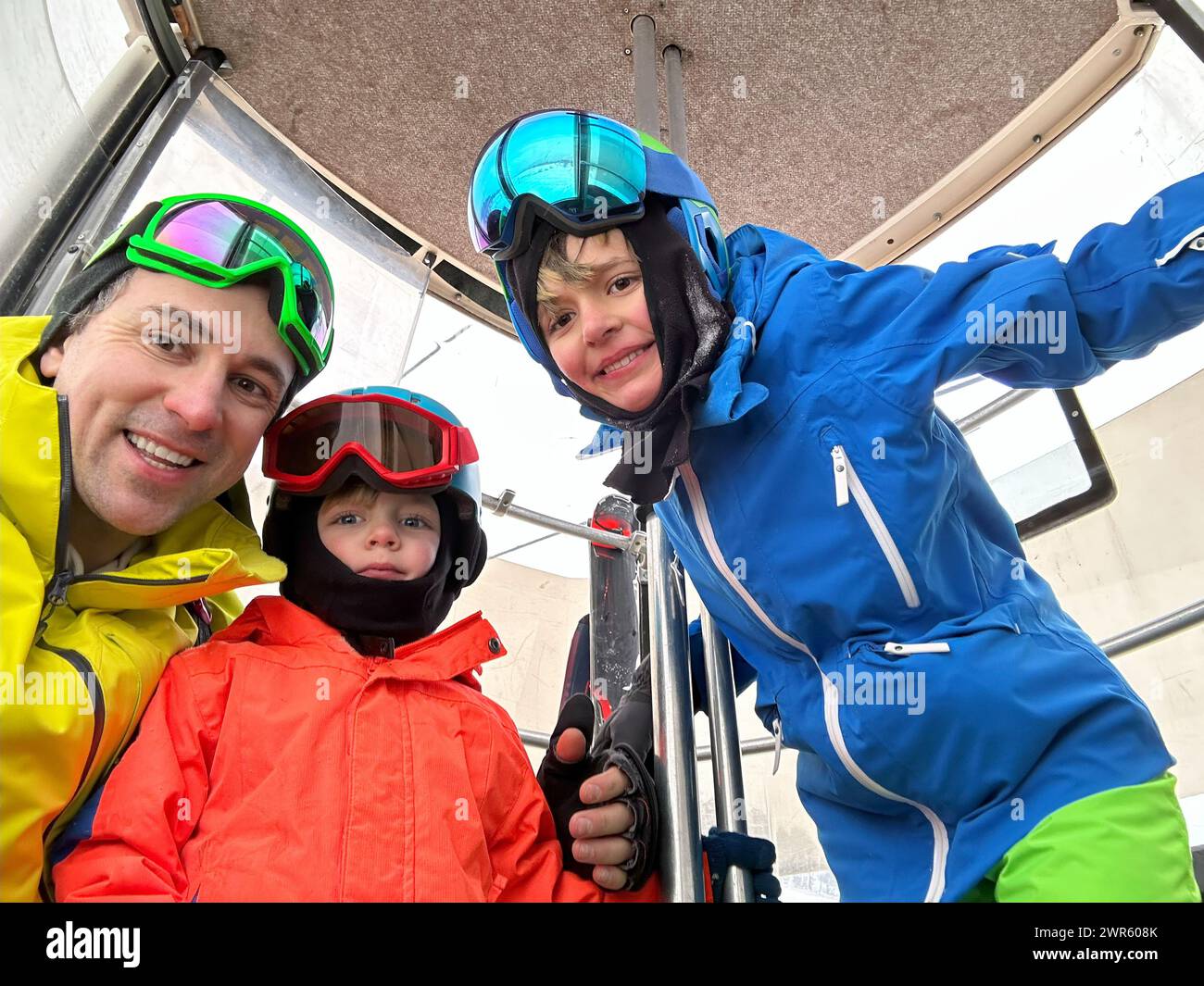 Inside a ski lift three people, adult and two kids in skiing outfits ...