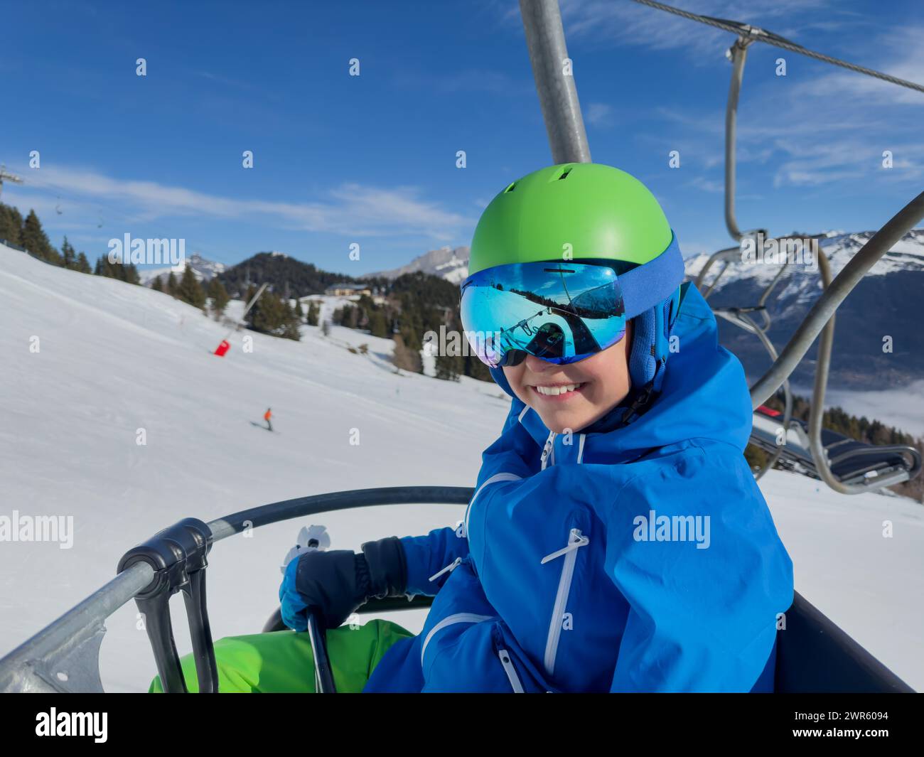 A ski lift carries a person in a bright helmet and blue jacket, set ...