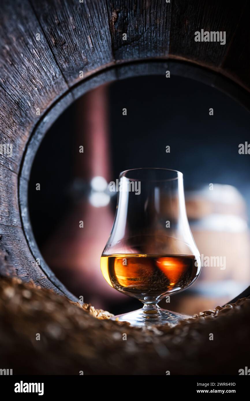 A glass of whiskey in old oak barrel. Copper alambic (distiller) on ...