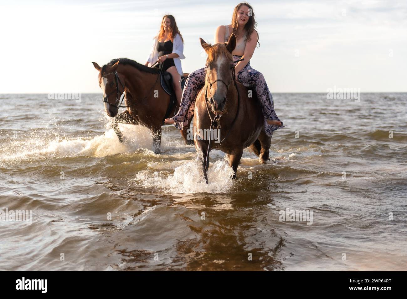Two women horseback riding in the ocean waves Stock Photo - Alamy