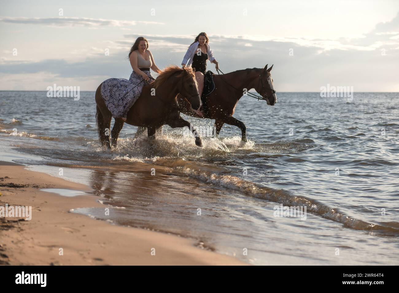 Two women on horseback riding in the ocean at sunset Stock Photo - Alamy